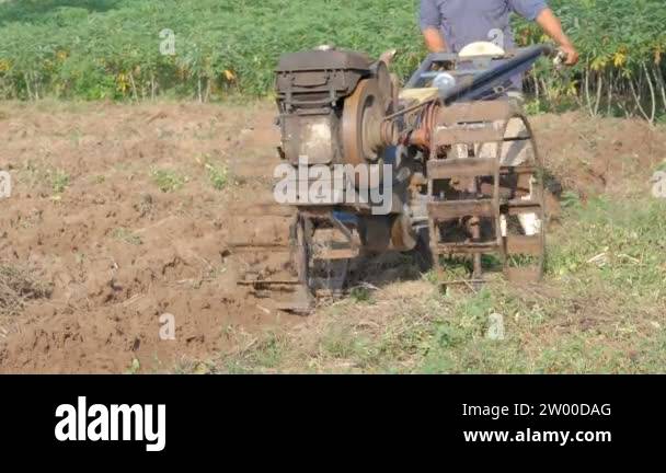 Old man using a small tractor to plow the farm to adjust the soil for ...