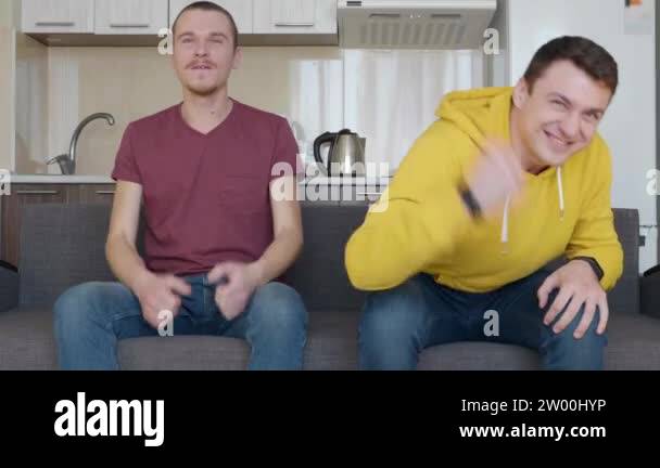 Two men sitting on the couch watch a football match on TV and enjoy the ...
