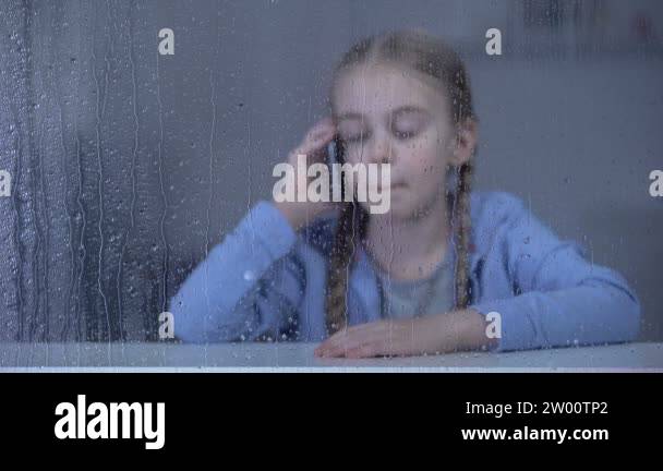Sad little girl talking phone on rainy day, staying home alone, missing ...