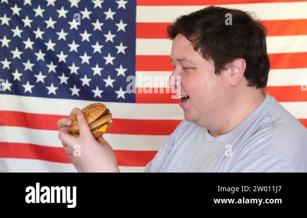 Fat man holding a piece of hamburger with an American flag background ...