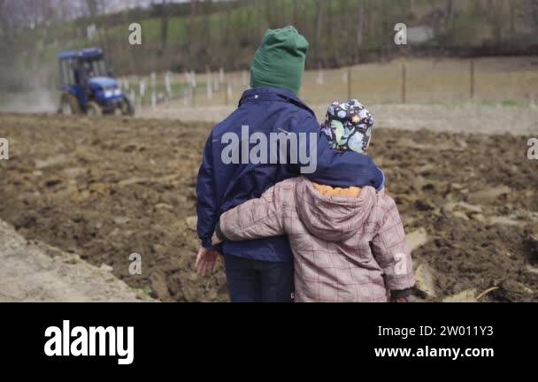 Two boys look how tractor cultivates the land for planting of the earth ...