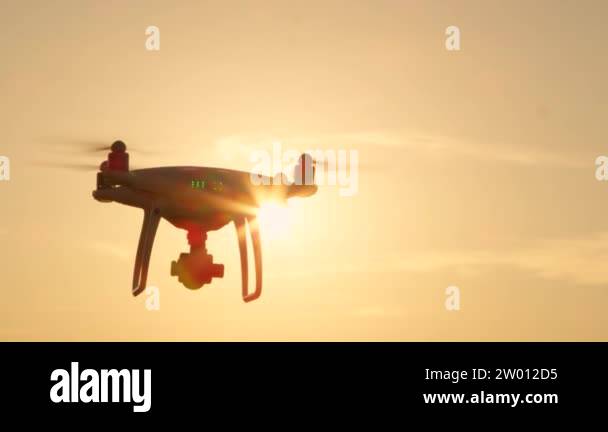 CLOSE UP LENS FLARE SILHOUETTE Small filming drone flying over golden ...