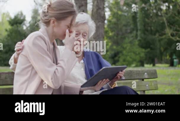 woman and senior grandmother using tablet device for video call at park ...