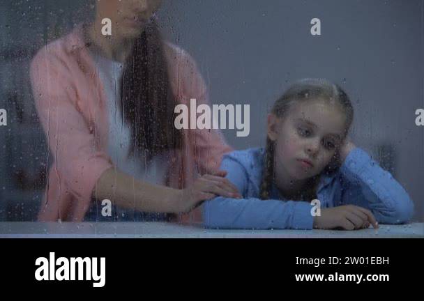 Mother supporting little girl behind rainy window, kid suffering from ...