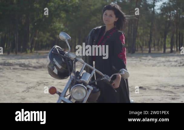 The girl with black hair standing at the motorcycle looking into the ...