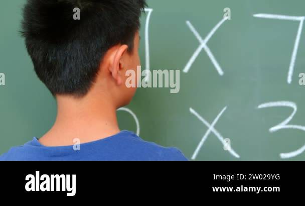 Rear view of Asian schoolboy solving math problem on chalkboard in ...