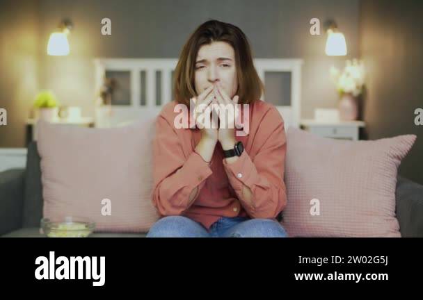 Sad young woman sitting on the sofa, eating popcorn, watching melodrama ...