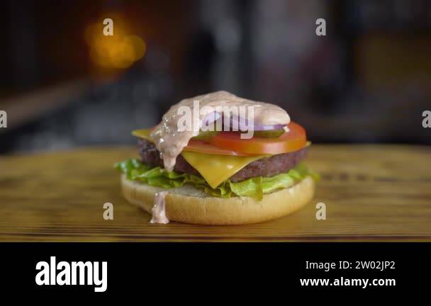 Spicy sauce drips from the juicy layers of unfinished burger in process ...