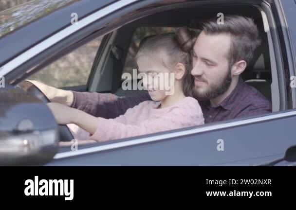 Little girl sitting on fathers lap in the car holding wheel close up ...