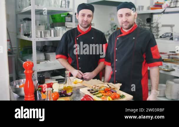 Restaurant kitchen. Two men chefs finished serving the dish, taking it ...