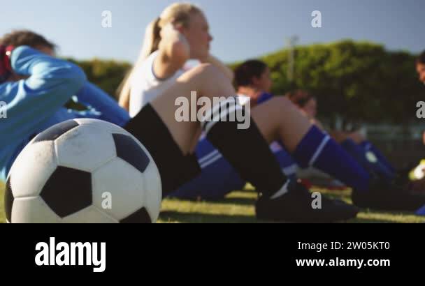 Side view of diverse female soccer team doing sit up exercises while ...