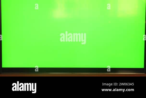 Female hand using a remote control to channels on flat green screen TV Watching television with ...