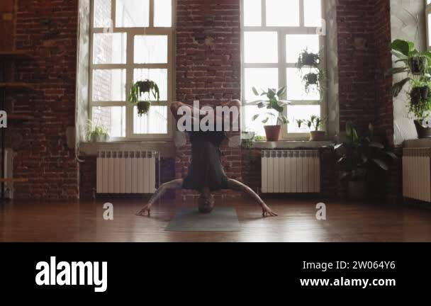 Hand standing pose. Young sporty man doing yoga in studio with wooden ...