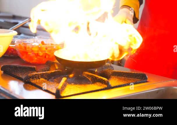 Male chef cooking flambe style dish on pan in modern kitchen of ...