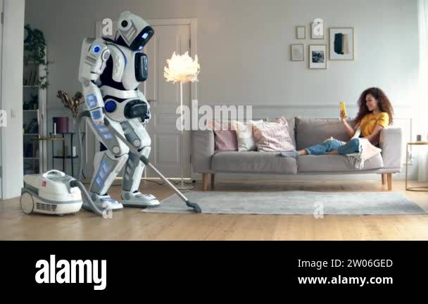 A robot does vacuum cleaning while a girl lying on a couch. Cyborg and ...