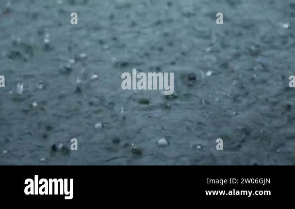 Rain drops fall on water surface of pond, lake or river forming a ...