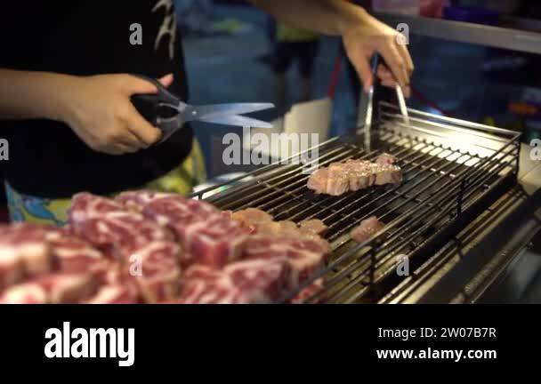 4k Vendor cooking a beef meat bits on steel grill in an Asian Night ...