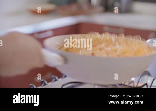 man hand detail cooking and tossing saute pasta spaghetti in pan.Young ...