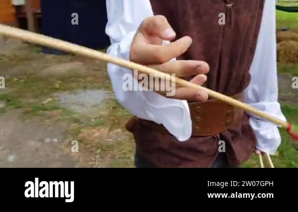 close-up a young guy in a medieval costume twists an arrow in a hand ...