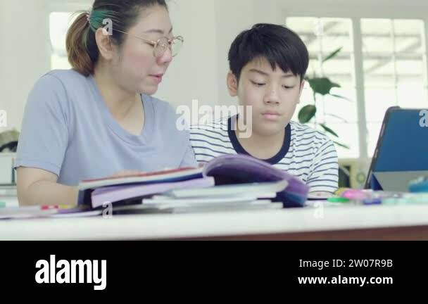 Mother helping her son to do his homework at home. Beautiful mother reading textbook and talking ...