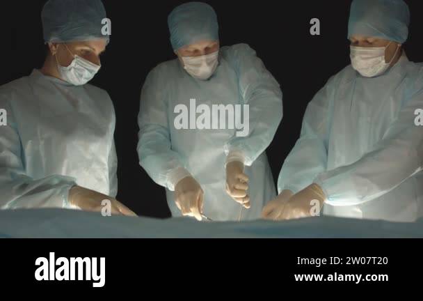 Three surgeons, a man and a woman, perform surgery in the operating ...