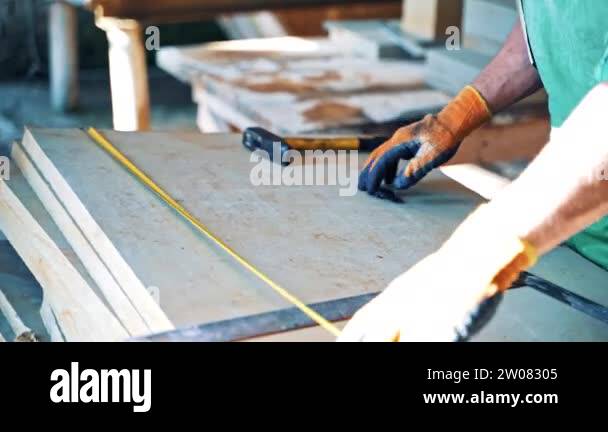 Worker in special uniform measures the stone slabs in factory. Man with ...