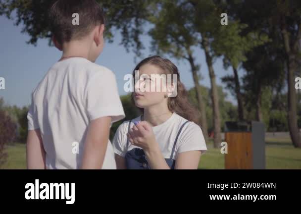 Strict older sister scolding her younger brother in the summer park ...