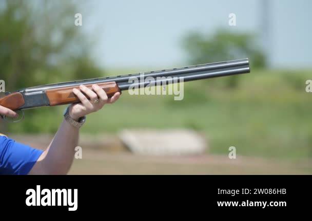Blue sky and a guy shooting from a double-barrel gun on a range in slo ...