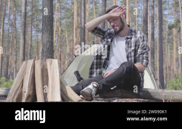 Young handsome man sitting in front of pieces of wood for the fire ...