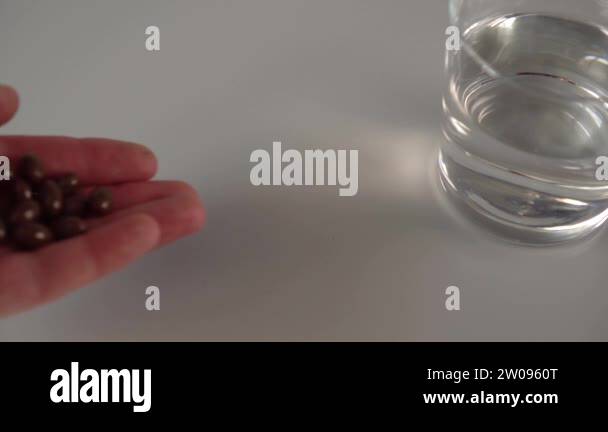 A hand spills a handful of dark brown medical capsules on a gray table ...