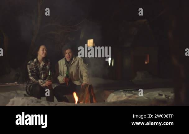 Young couple by the fire with beer.Girl and man sit with bottles of ...