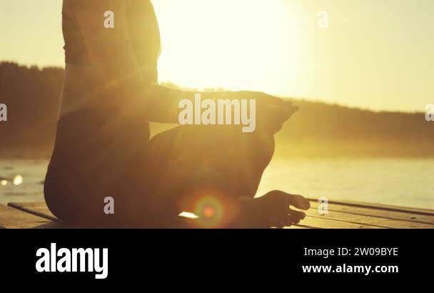 Young woman meditating in Lotus pose on river pier at yellow sunset ...
