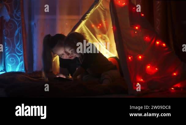 Bedtime story. Happy mother and little son read a book in a tent at ...