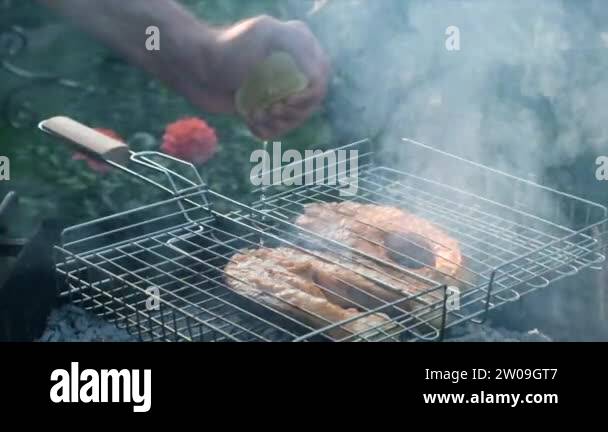 Human hand squeezing lime juice on fish on the lattice on barbecue ...