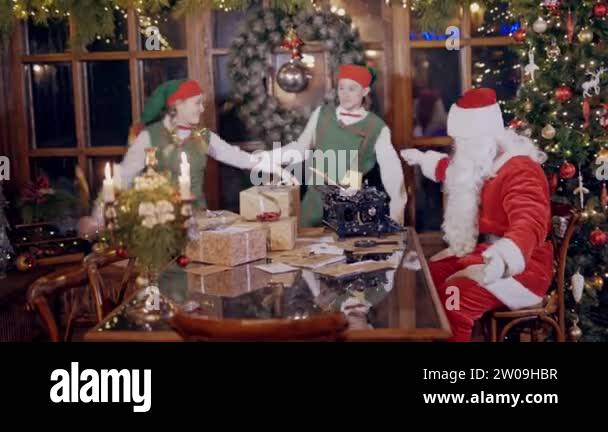 Two merry elves in costumes are dancing together and Santa shows them ...
