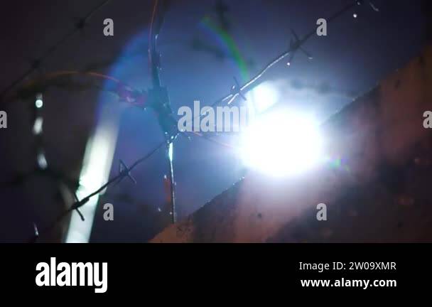 Close-up of bright light shining through barbed wire at night. Footage ...