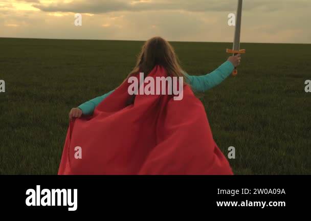 free girl in a red cloak runs with swords in his hand across field ...