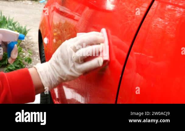 Woman in red clothes washes dirty red car by hand with sponge and soapy ...