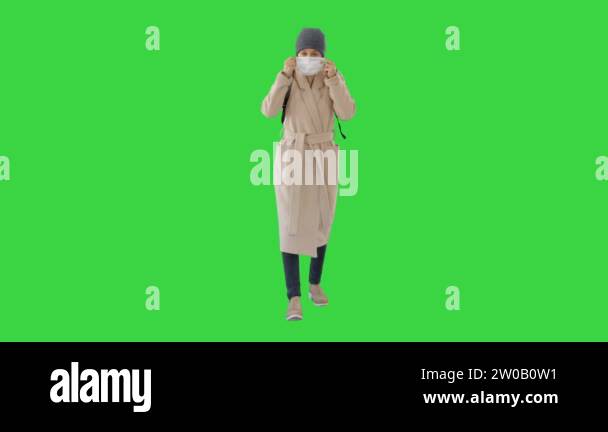 Woman dressed in a coat wearing putting on protective face mask on a ...