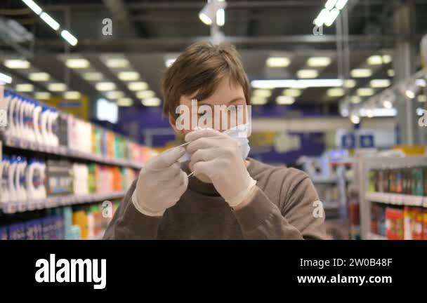 Man in a medical mask and rubber gloves in a supermarket removes the ...
