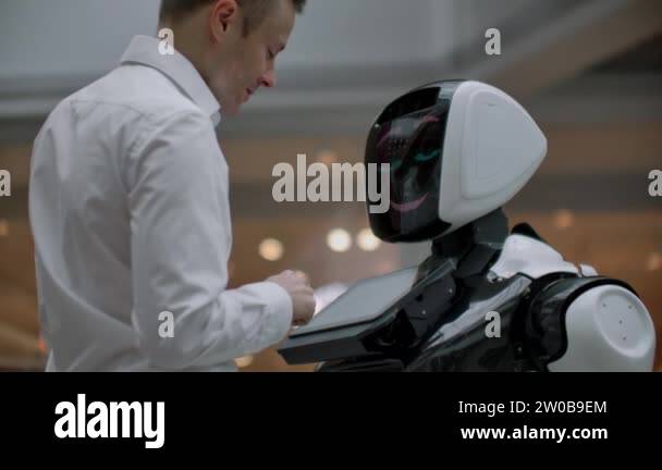 A man stands with a robot bot and asks him questions and asks for help ...