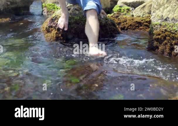 Men's feet are washed by sea waves. The barefoot of the guy stands on a ...