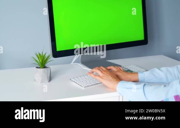 Woman typing on a computer keyboard, monitor with a green screen ...
