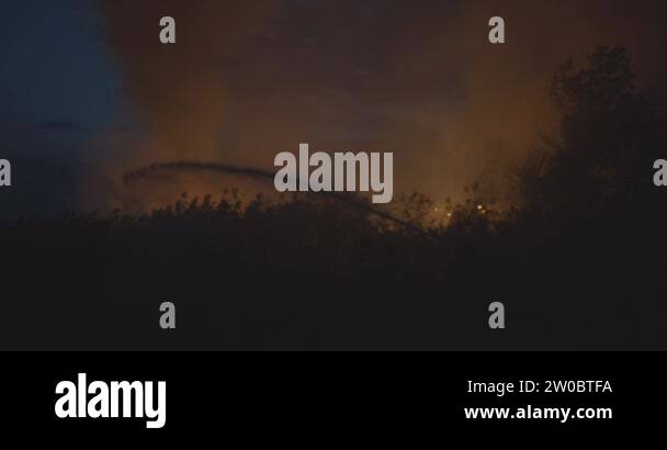 Burning grass on field at the night. Firefighters fighting a fire with ...