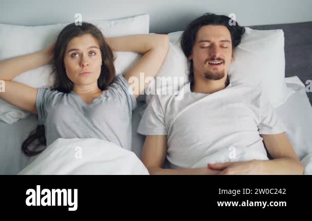 Angry wife covering face with pillow while sleeping husband snoring in ...