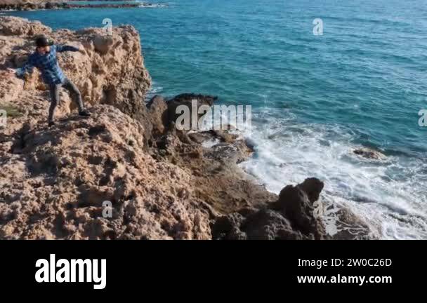 Young guy stands on rocks and throws stones into water. Caucasian boy ...