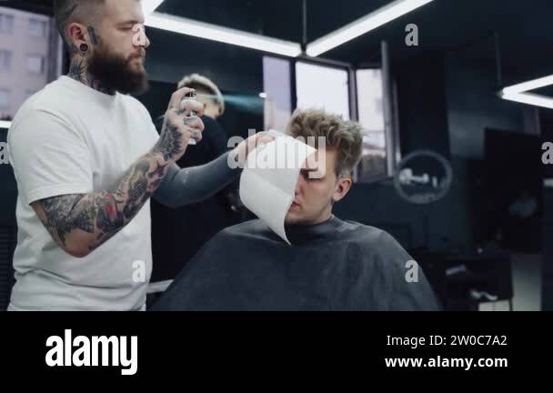 Attractive male is getting a modern haircut in barber shop. Barber dyes ...