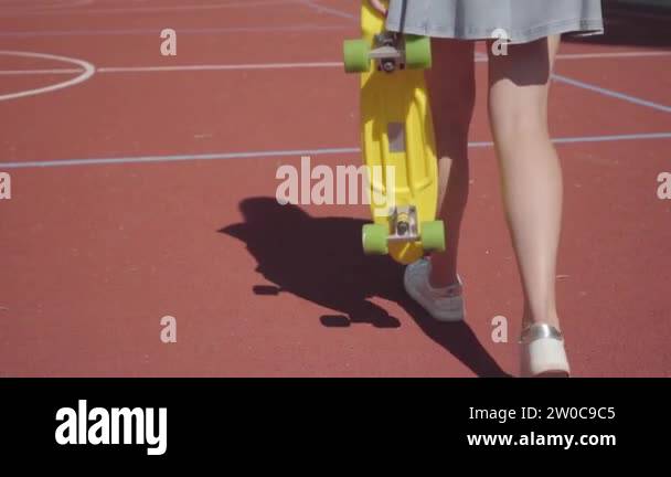 Legs woman in short skirt with a yellow skateboard walking on the ...