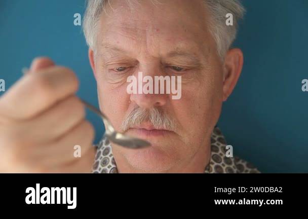 A senior man responds to a spoonful of bad-tasting cough syrup Stock ...