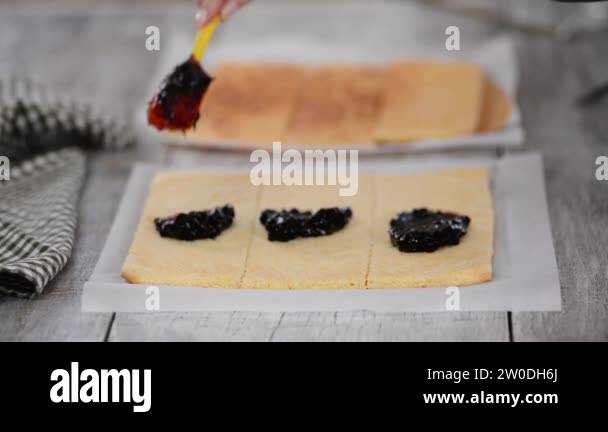 Girl spreading jam on a flat sheet of cake to make a cake with vertical ...